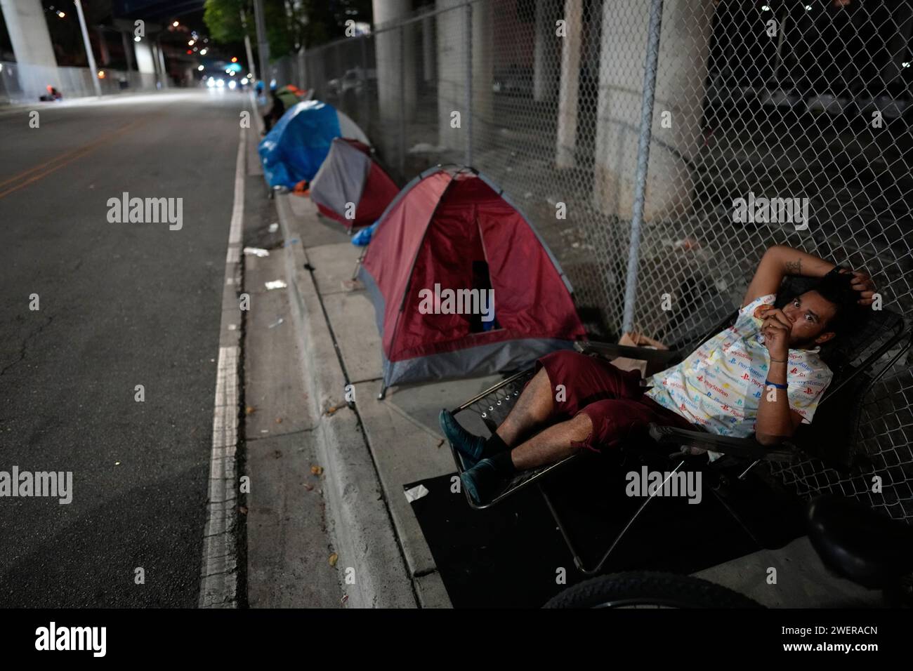 A person rests in a lounge chair on a sidewalk alongside tents as a ...