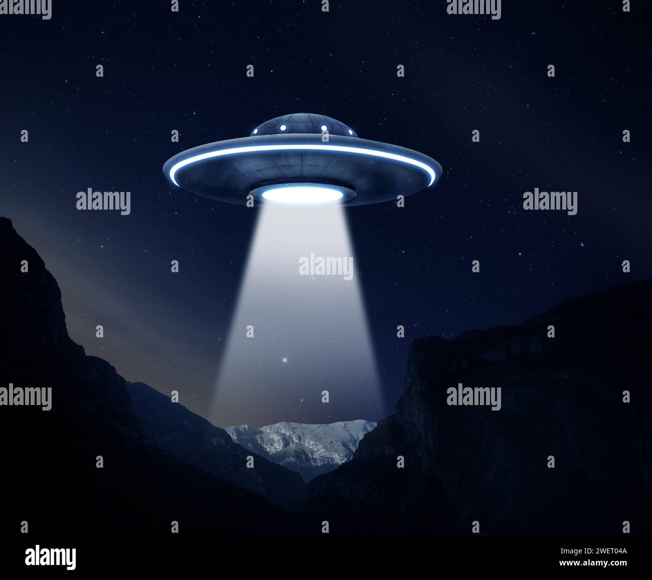 UFO. Alien spaceship emitting light beam over mountains at night ...