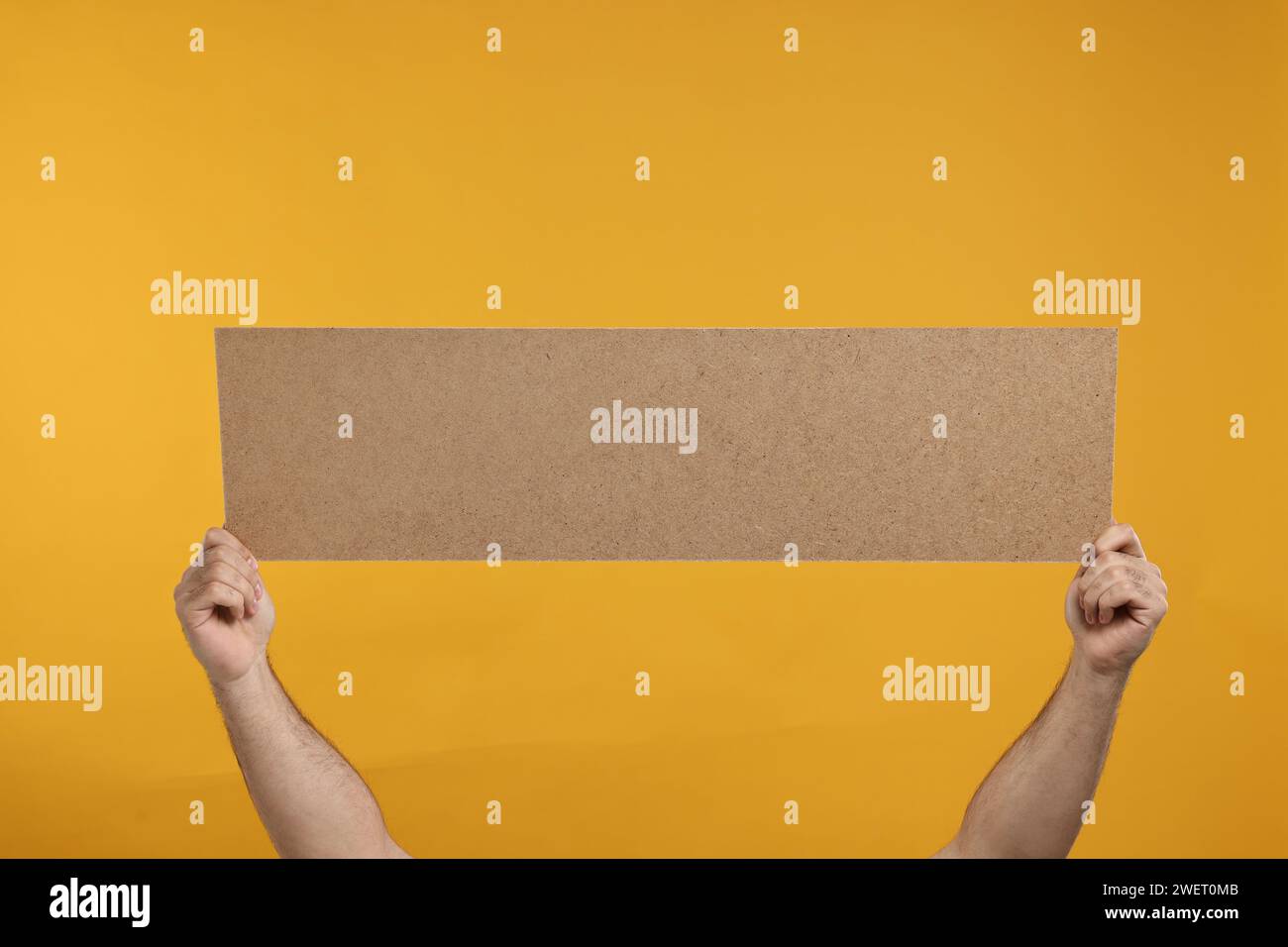 Man holding blank cardboard banner on orange background, closeup. Space ...