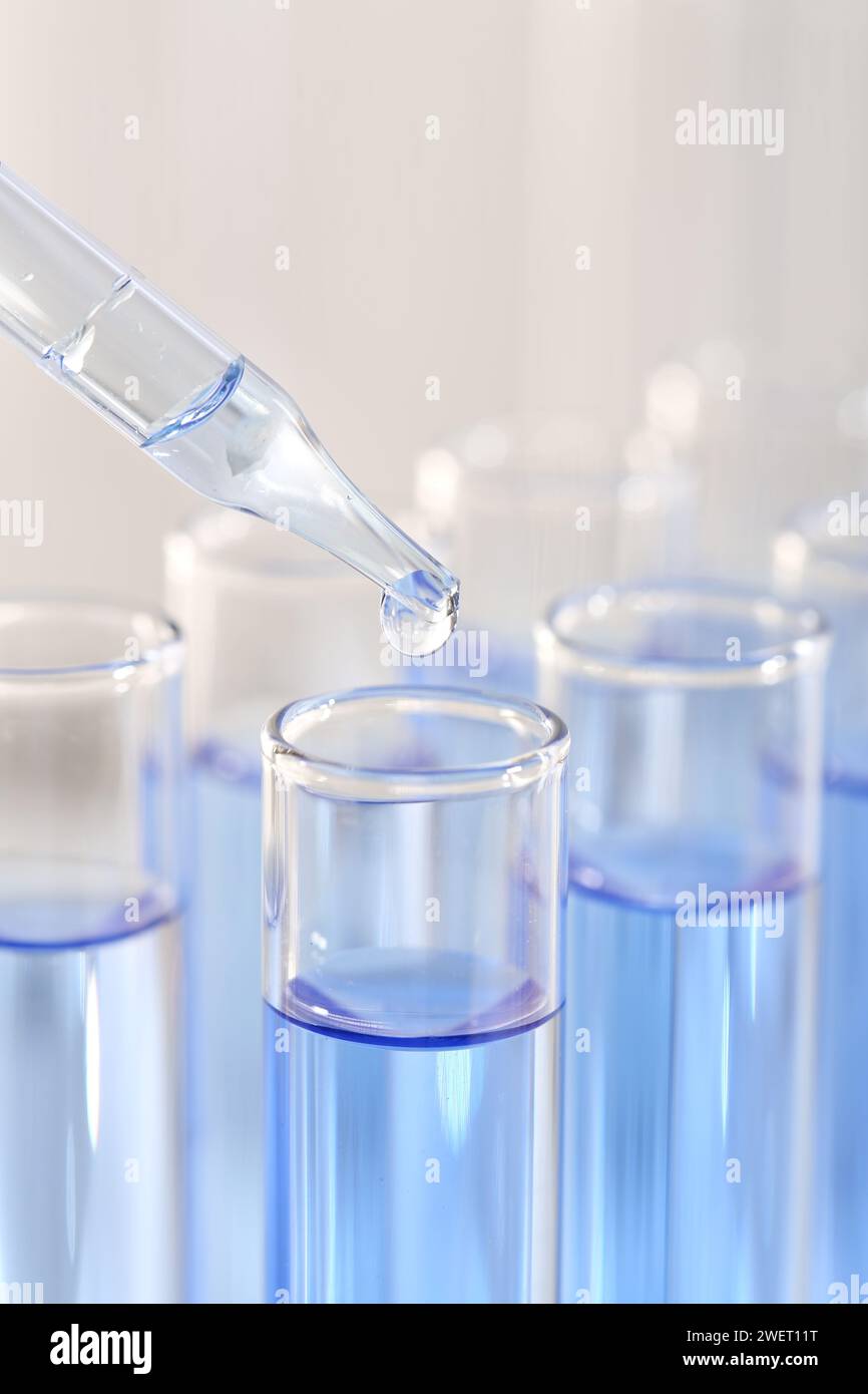 Laboratory analysis. Dripping light blue liquid from pipette into glass ...