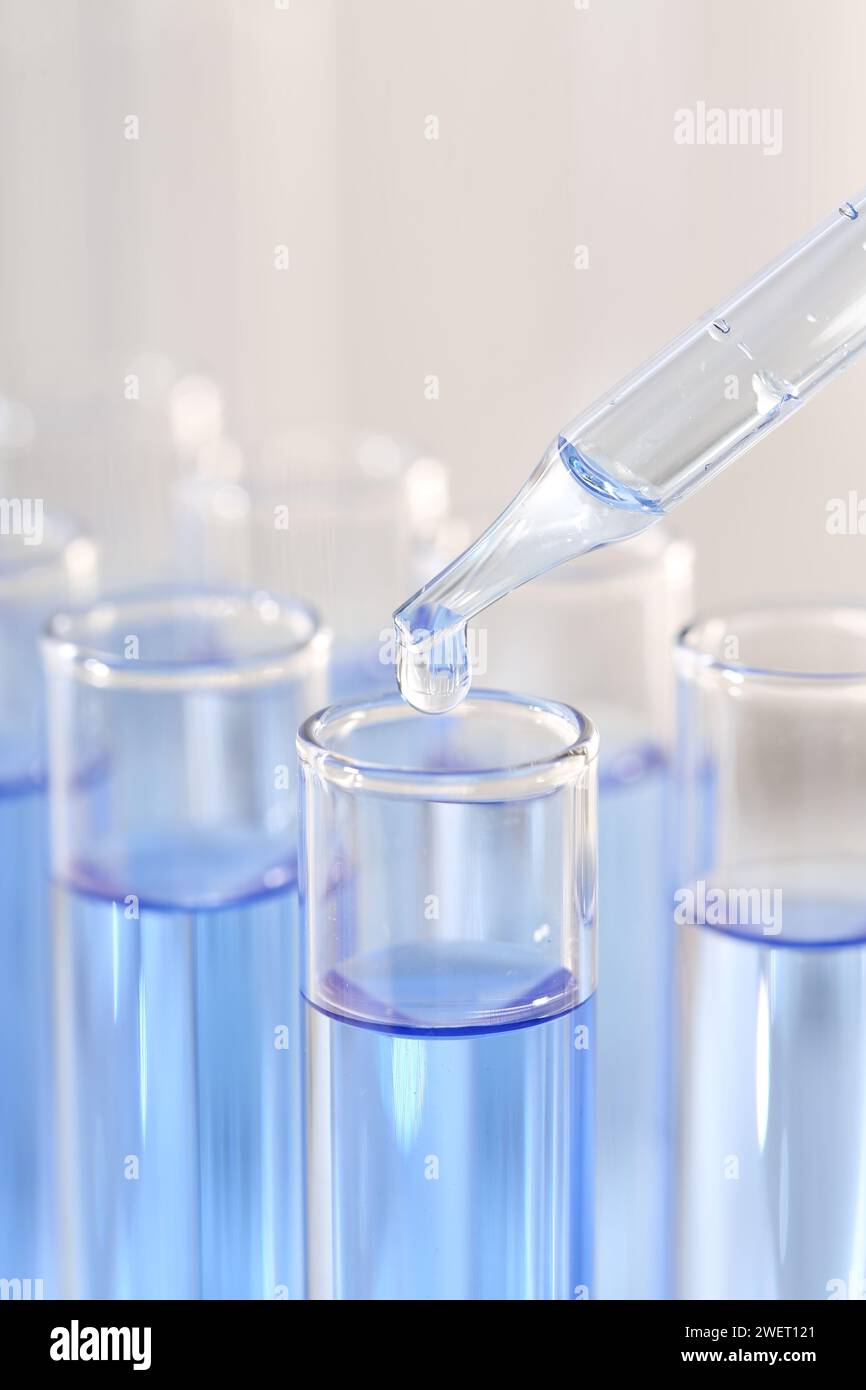 Laboratory analysis. Dripping light blue liquid from pipette into glass ...