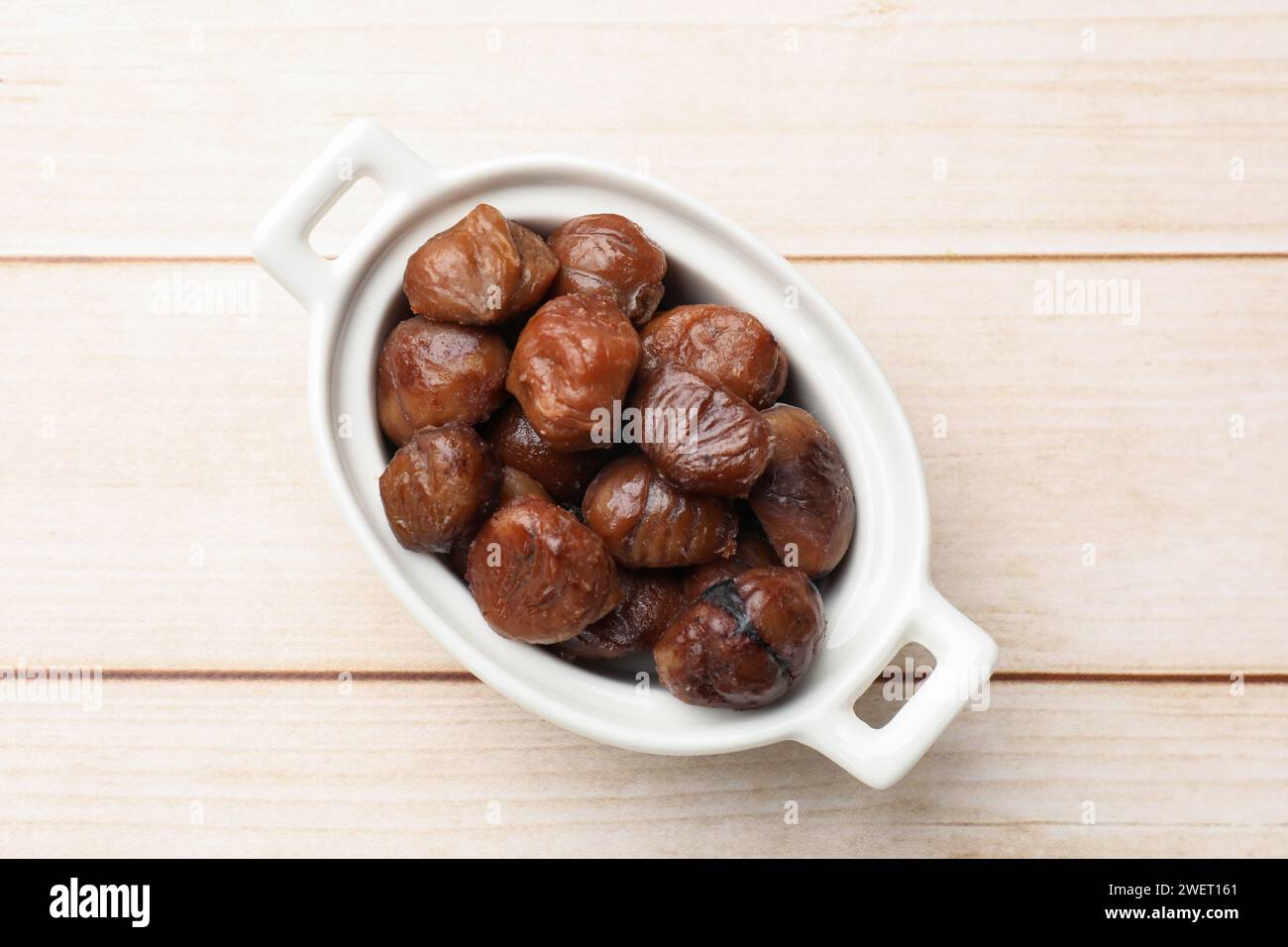 Roasted edible sweet chestnuts in dish on light wooden table, top view ...