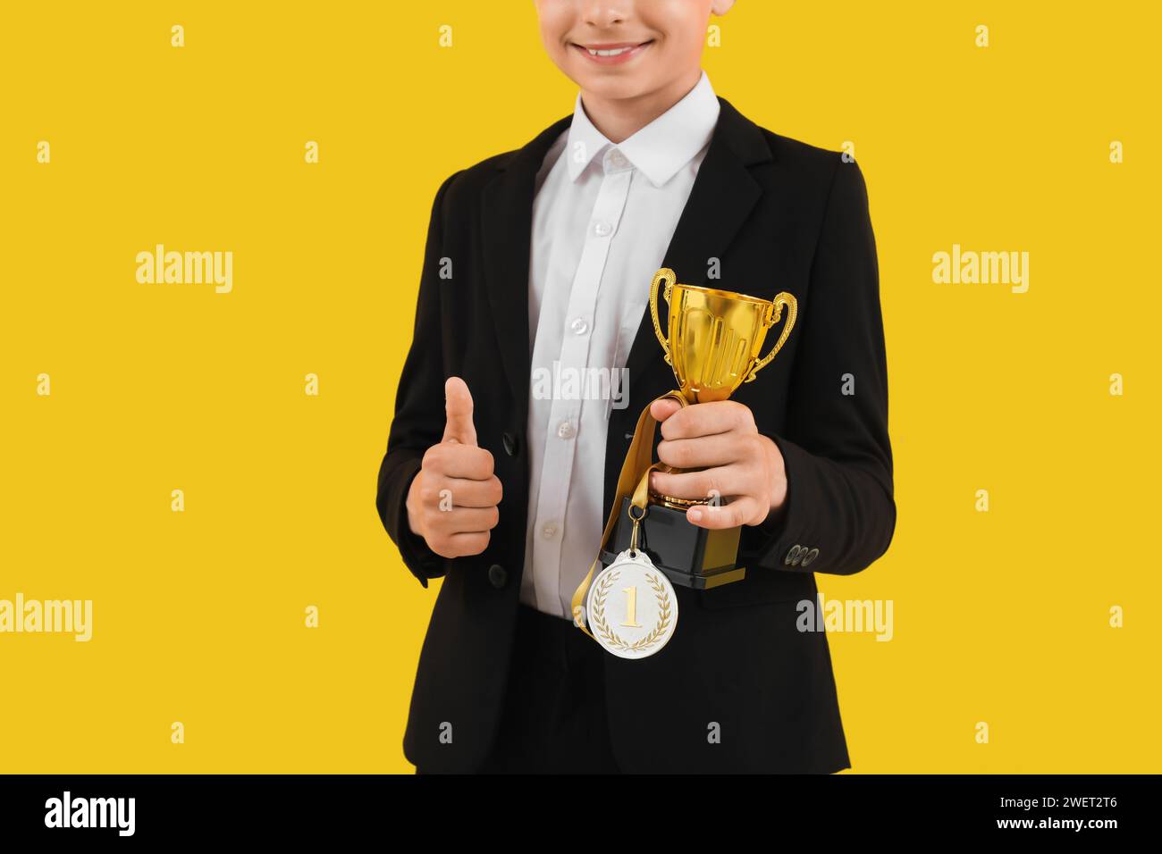Smart little school boy with prize cup and medal showing thumb-up ...