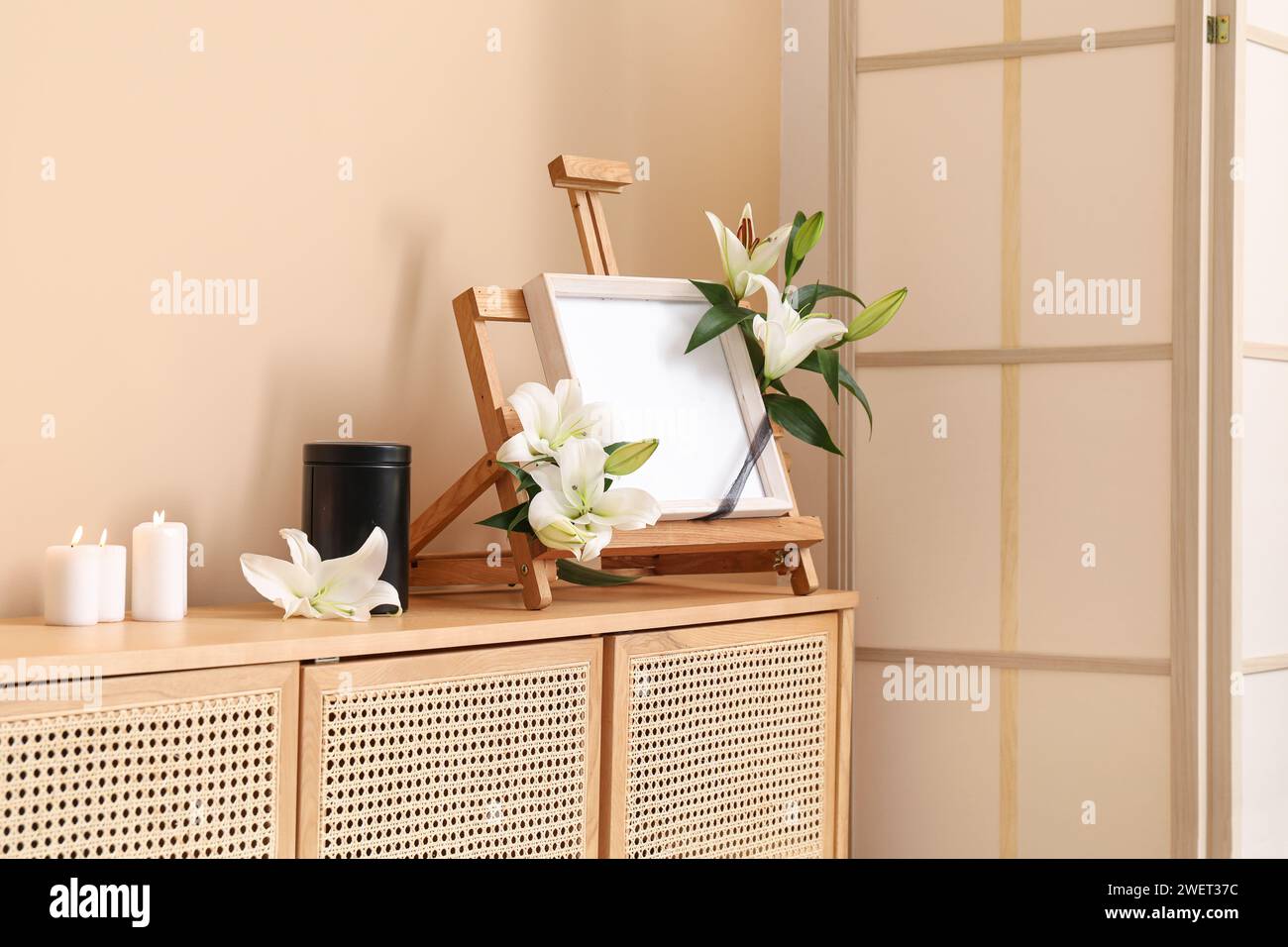 Blank funeral frame with lily flowers, mortuary urn and burning candles ...