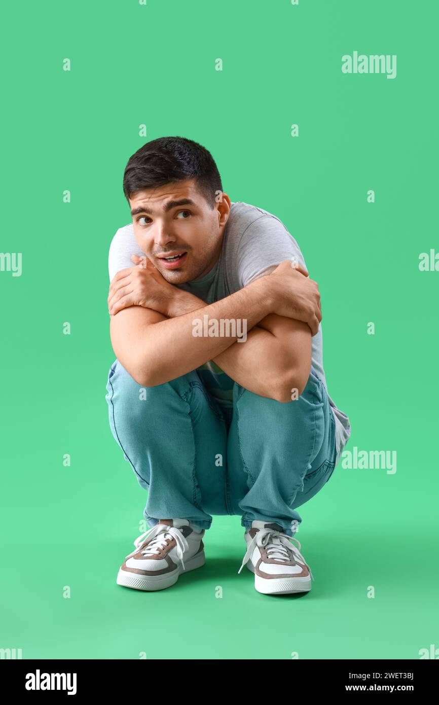 Afraid young man sitting on green background Stock Photo - Alamy