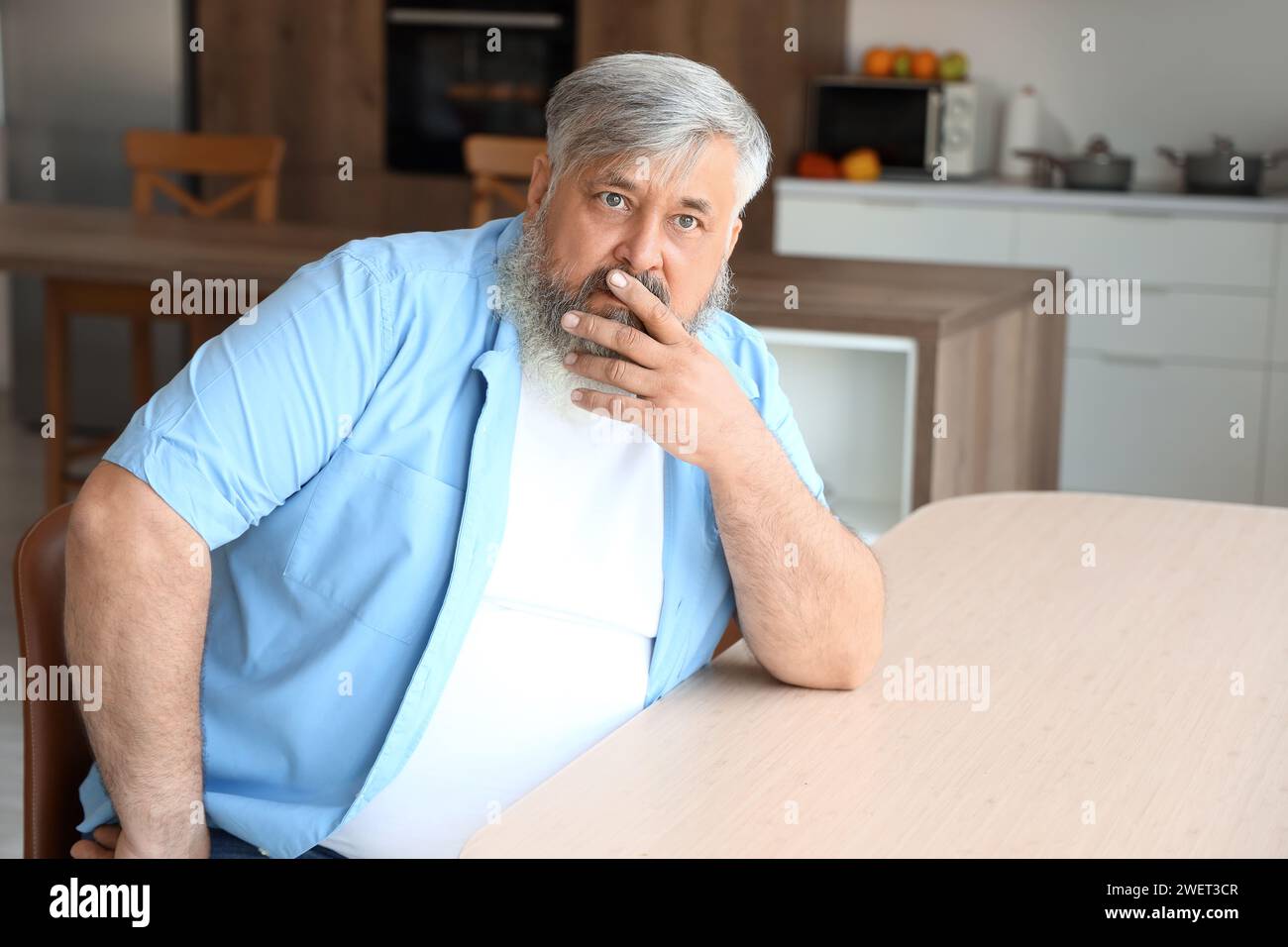Afraid mature man at table in kitchen Stock Photo - Alamy