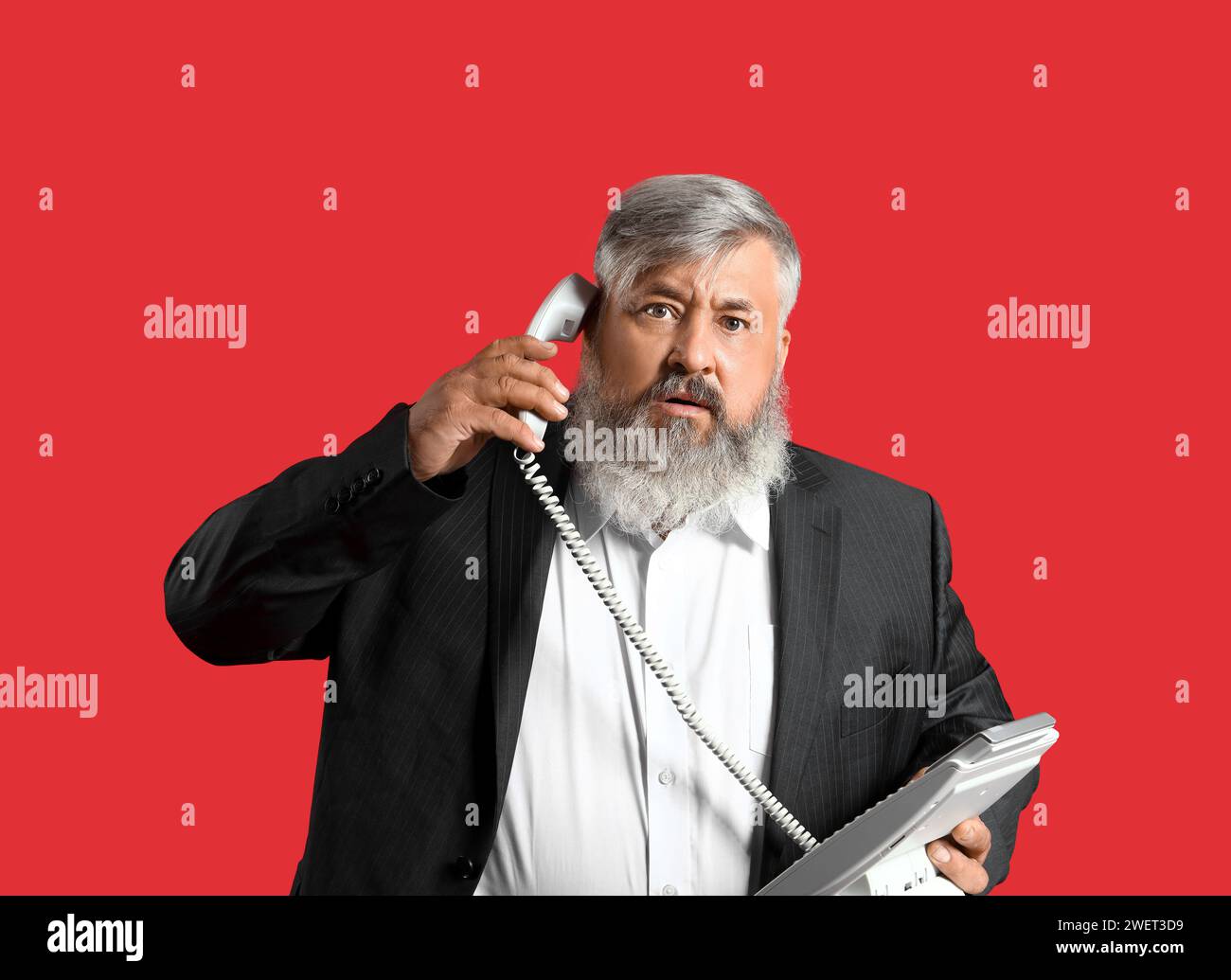 Afraid mature man with landline phone on red background Stock Photo - Alamy