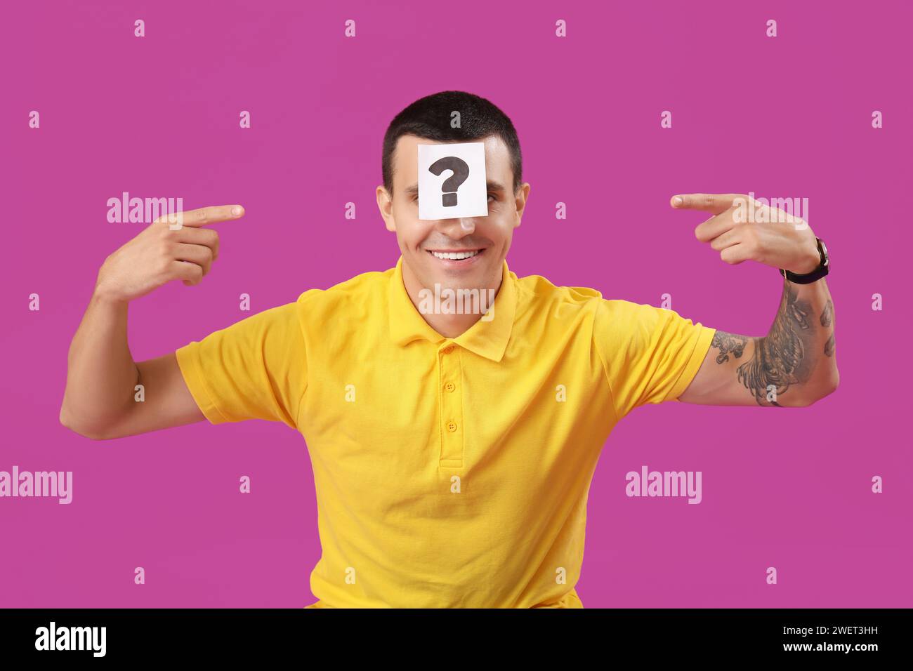 Young man pointing at paper question mark on his forehead against ...