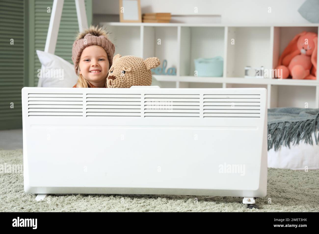 Cute little girl with toy bear warming near radiator in bedroom Stock ...