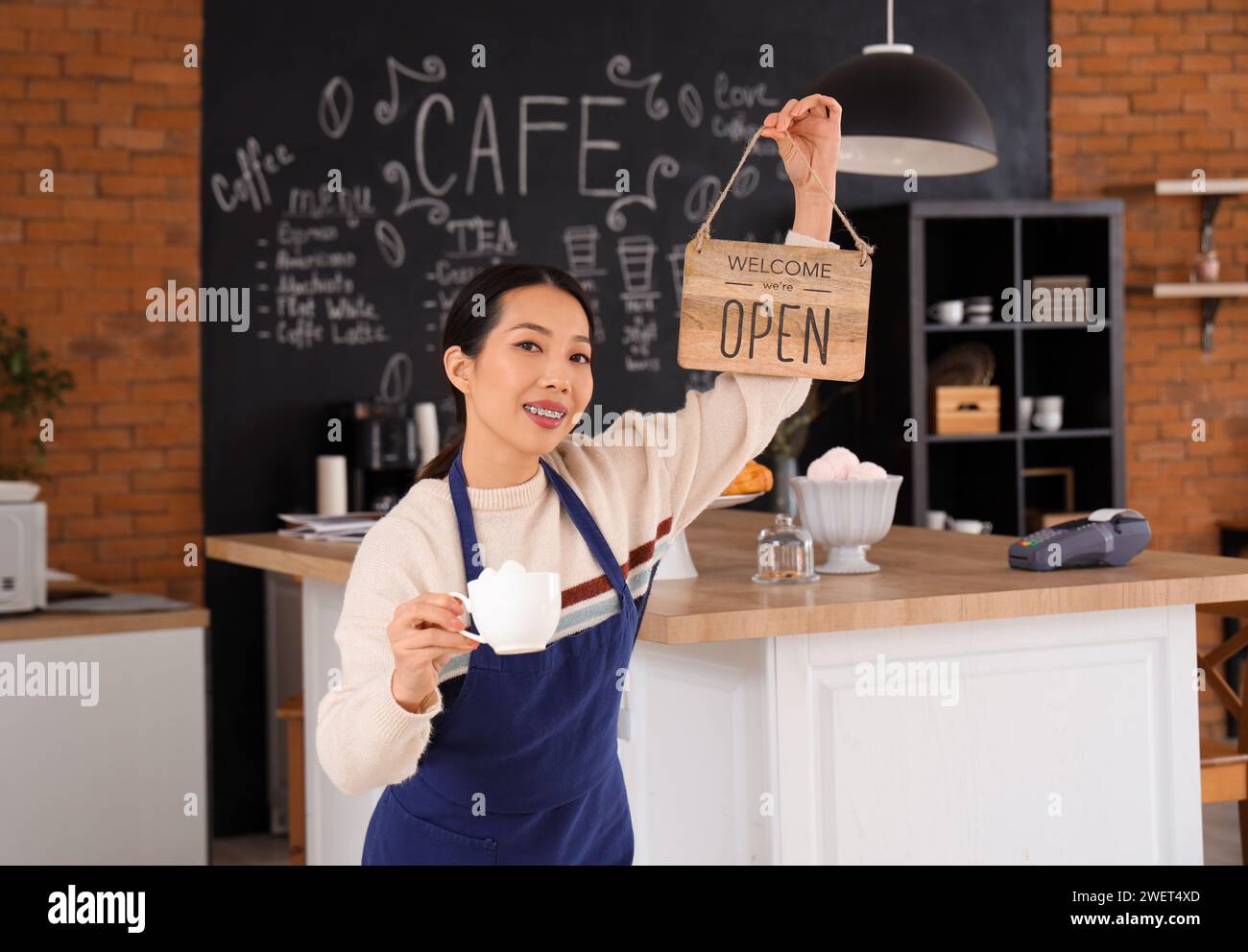 Female Asian barista with cup and OPEN sign in coffee shop Stock Photo ...
