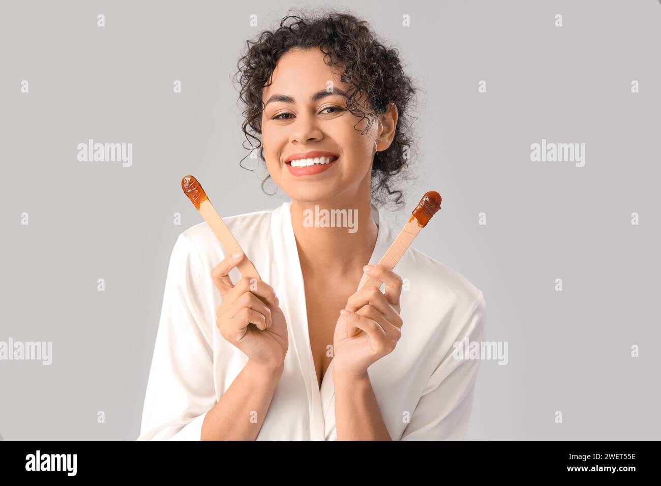 Beautiful African-American woman with sugaring paste on grey background ...