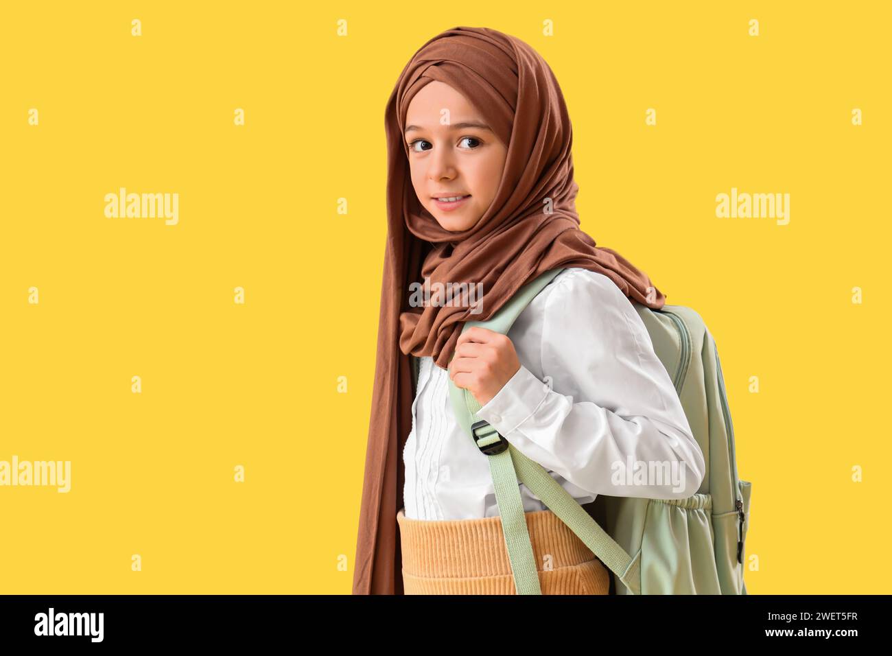 Little Muslim girl in hijab with school backpack on yellow background ...