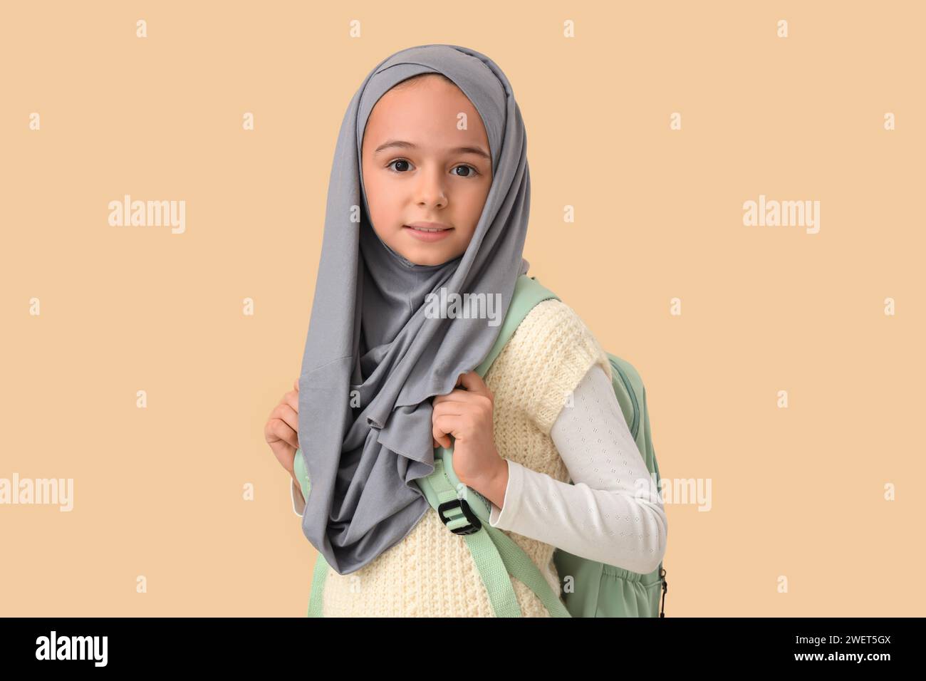 Little Muslim girl in hijab with school backpack on beige background ...
