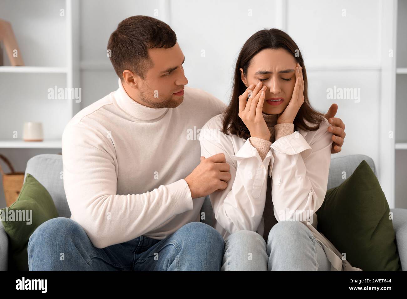 Young man hugging his crying wife on sofa at home Stock Photo - Alamy