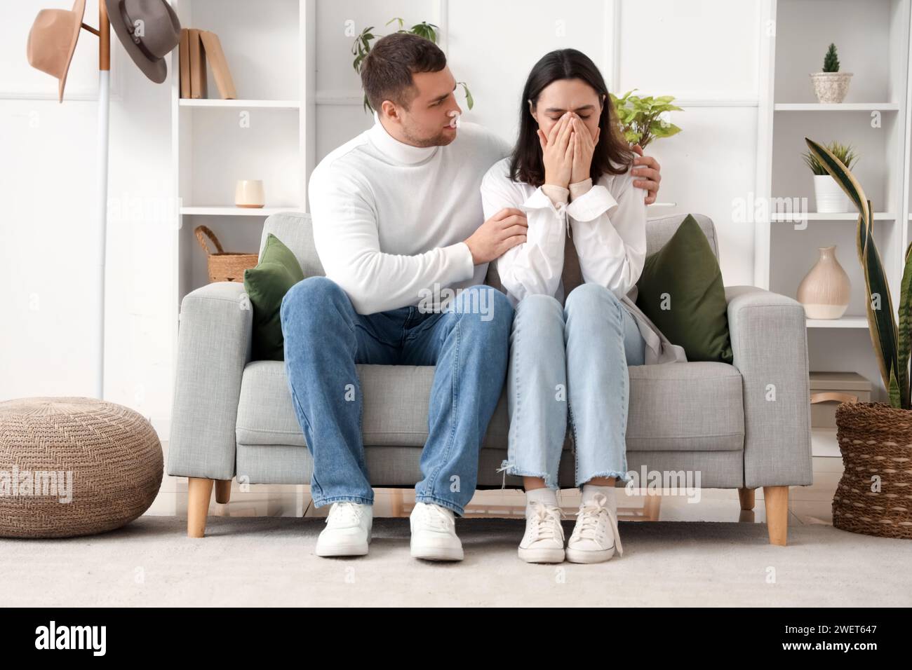 Young man hugging his crying wife on sofa at home Stock Photo - Alamy