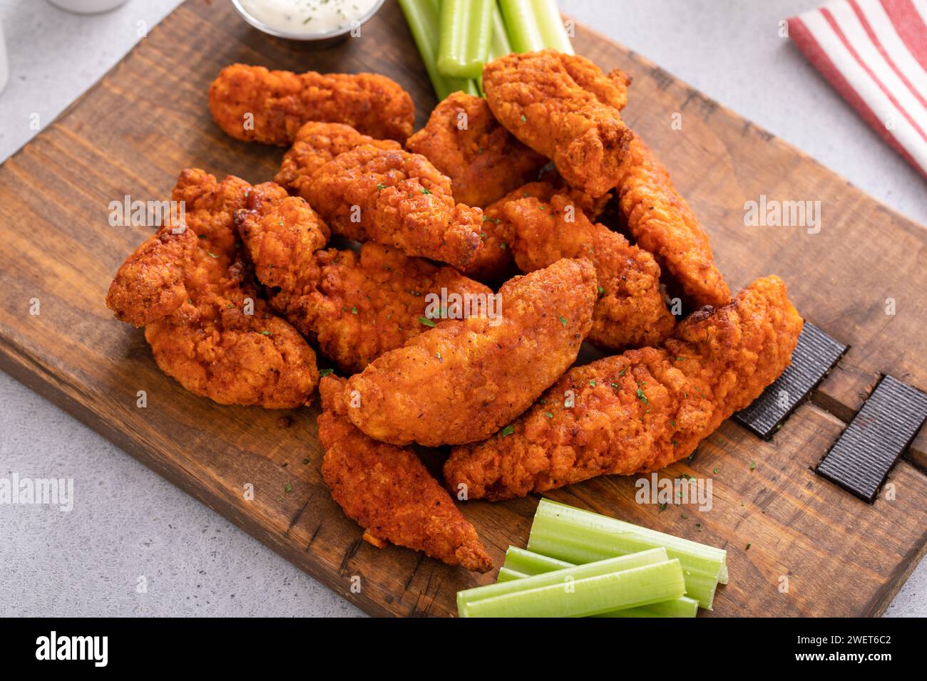 Buffalo fried chicken strips on a board with ranch and celery sticks ...