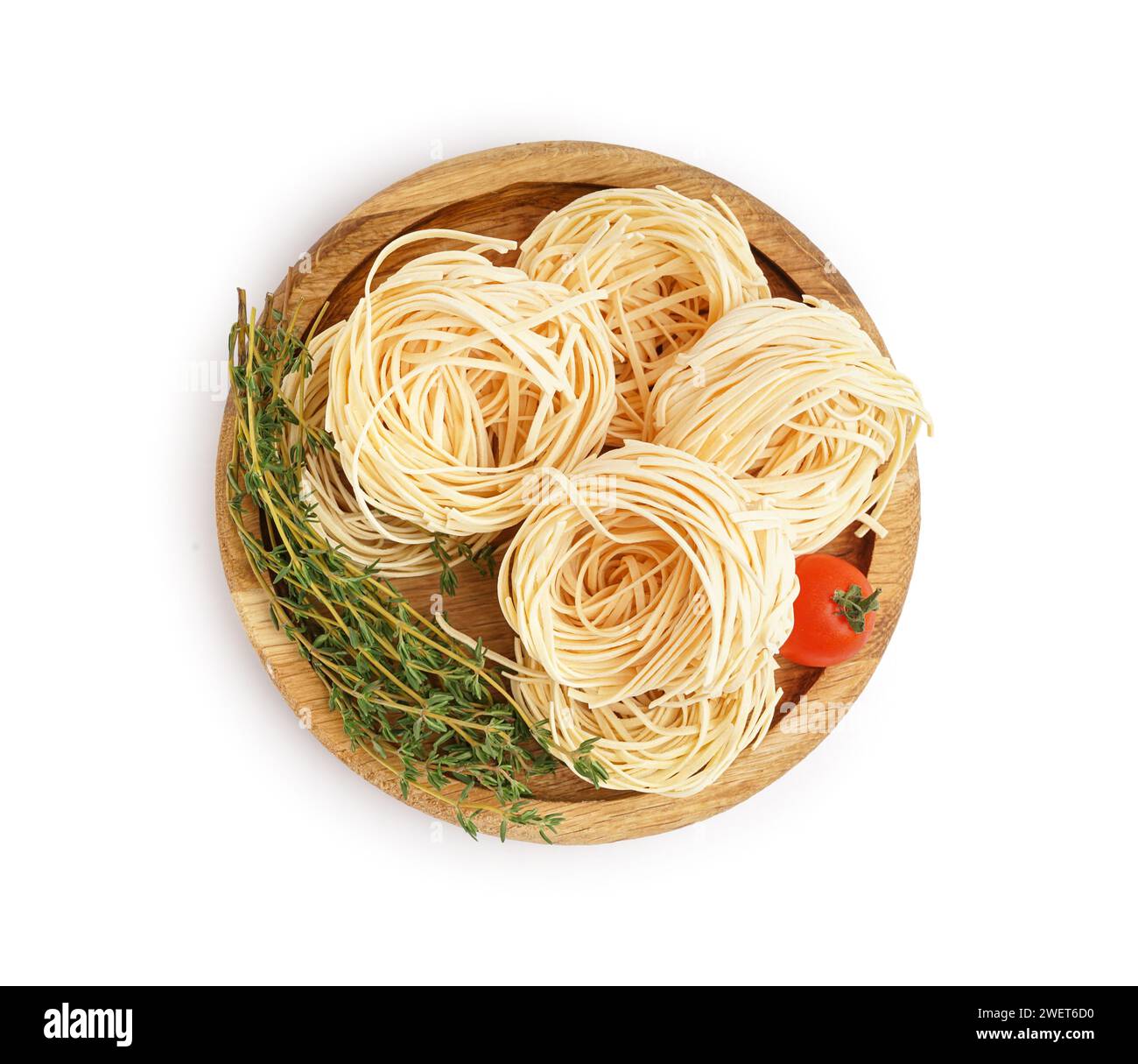 Wooden plate with raw pasta nests, thyme and tomato on white background ...