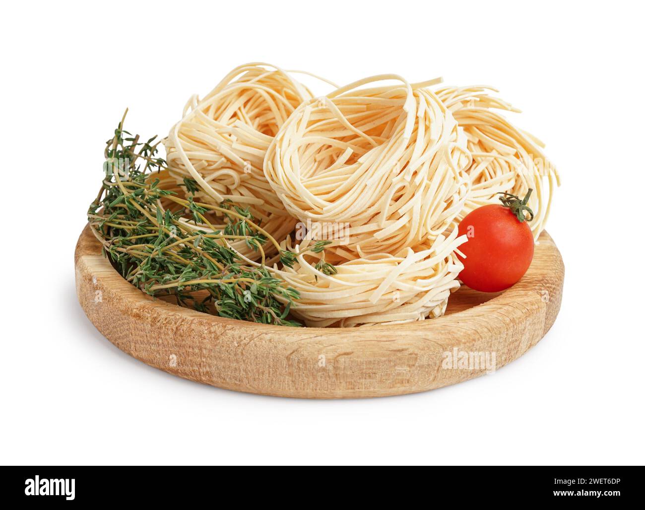 Wooden plate with raw pasta nests, thyme and tomato on white background ...