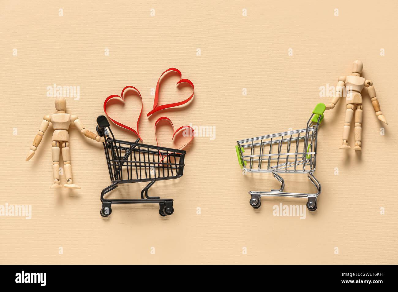 Small shopping carts with wooden human figurines and hearts on beige ...
