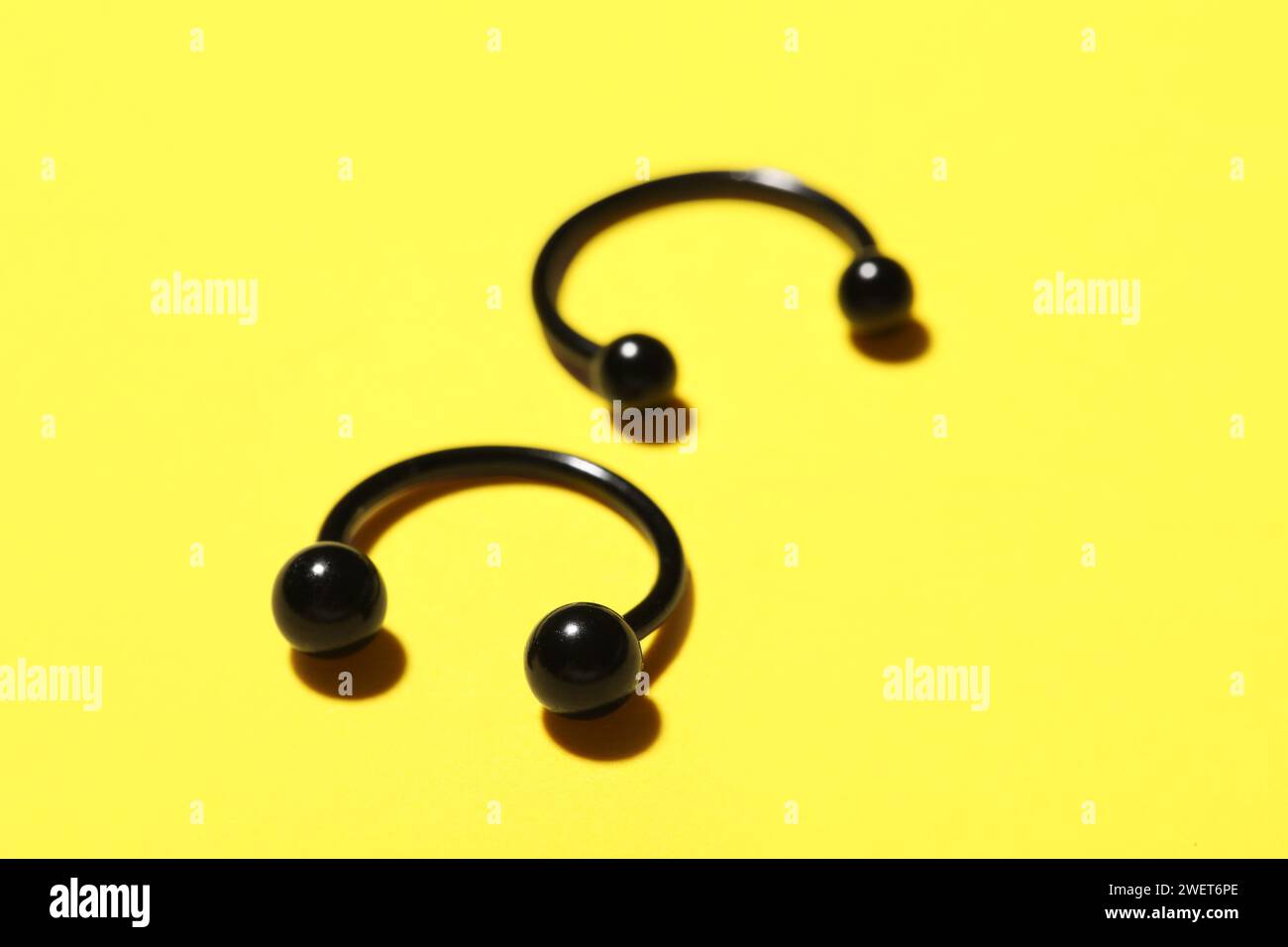 Circular barbells for piercing on yellow background Stock Photo - Alamy