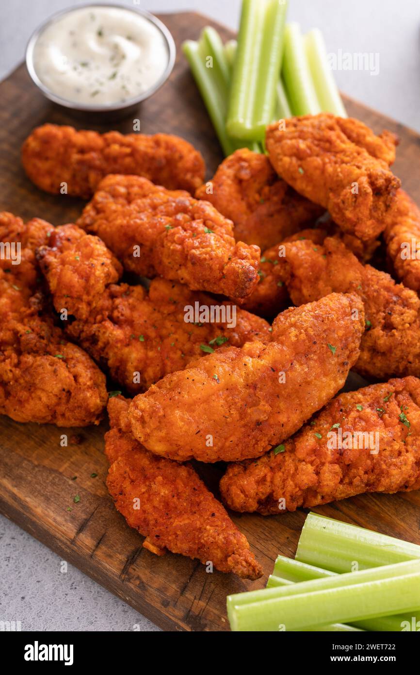 Buffalo fried chicken strips on a board with ranch and celery sticks ...