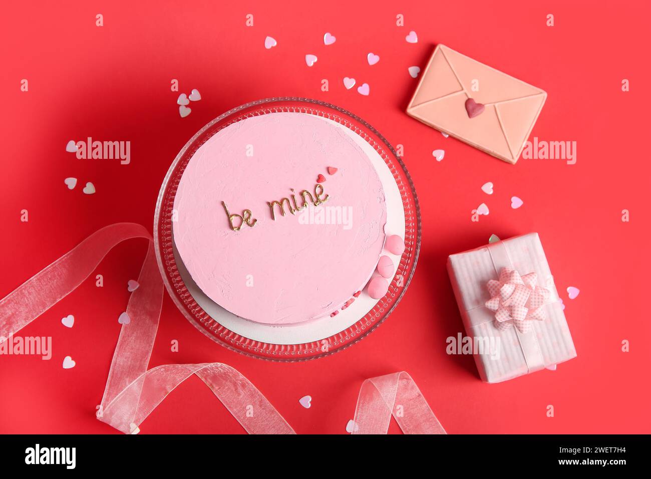 Stand with pink bento cake, gift box and cookie on red background ...