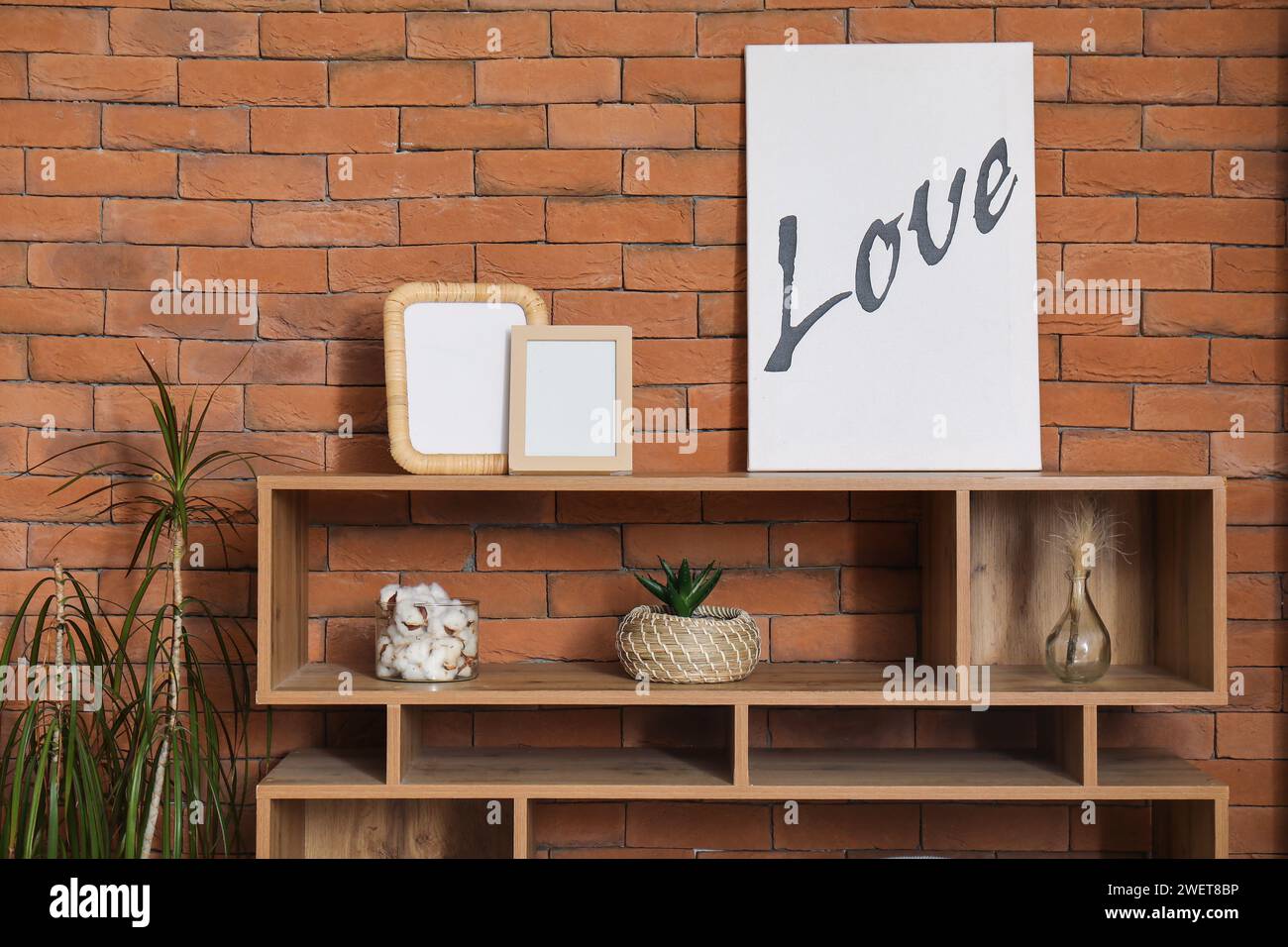 Modern shelving unit with poster and blank frames near brick wall Stock ...