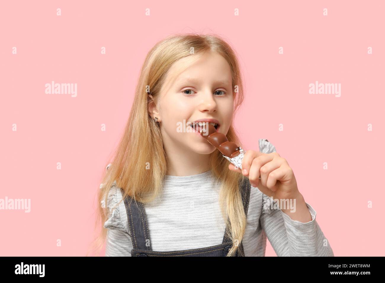 Cute little girl eating sweet chocolate on pink background Stock Photo ...
