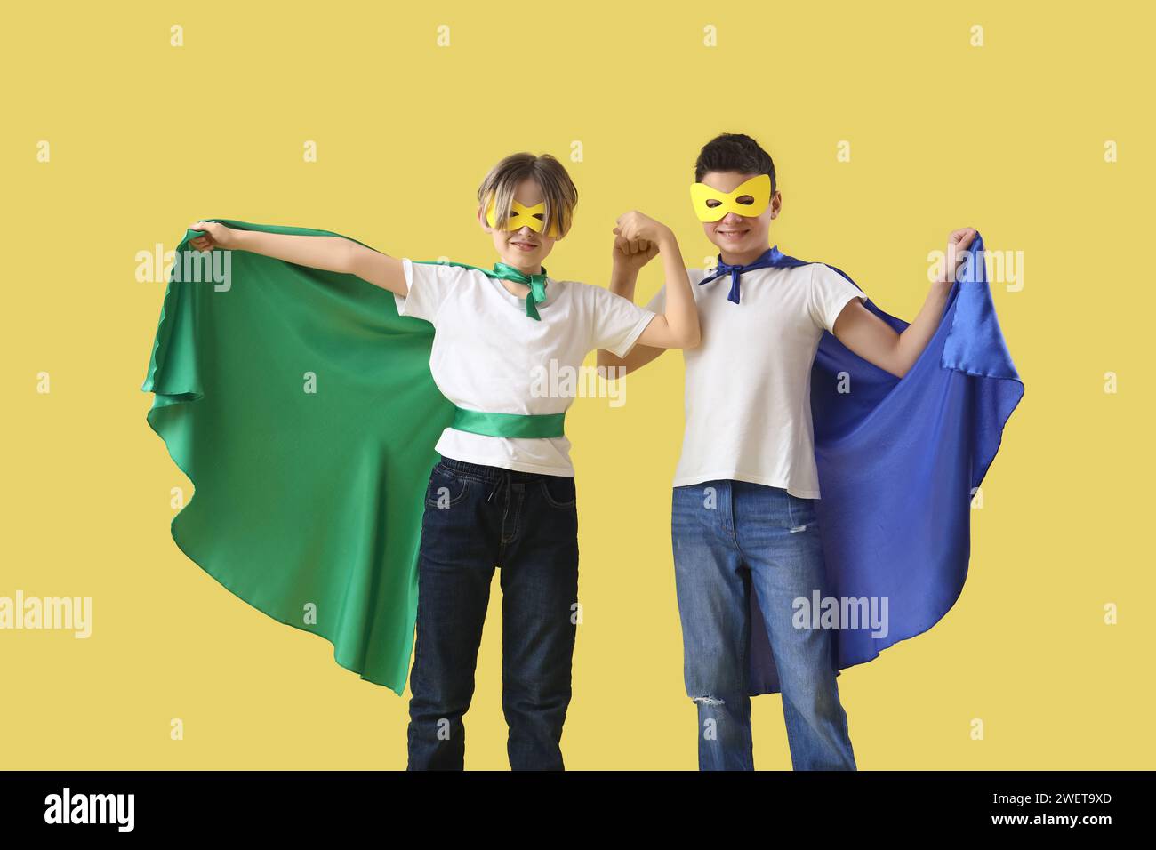 Happy brothers dressed as superheroes showing muscles on yellow ...