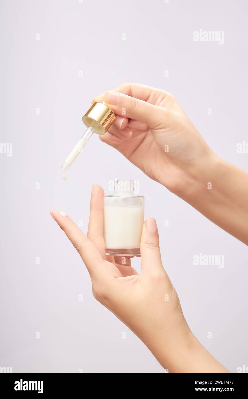 Female hands holding a white serum bottle without label, dripping of ...