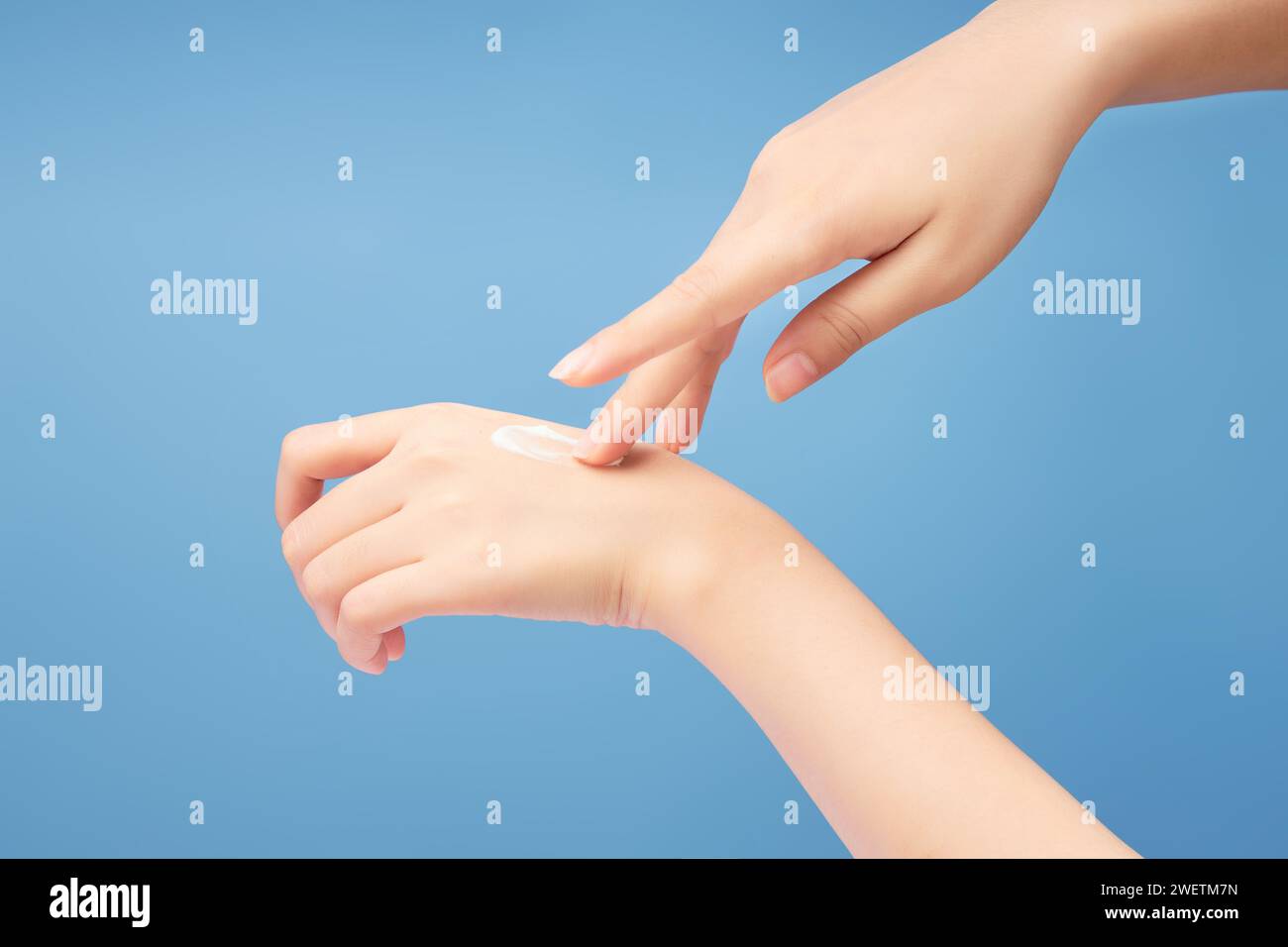 Woman's hand applying cream on the back of her other hand on a blue ...