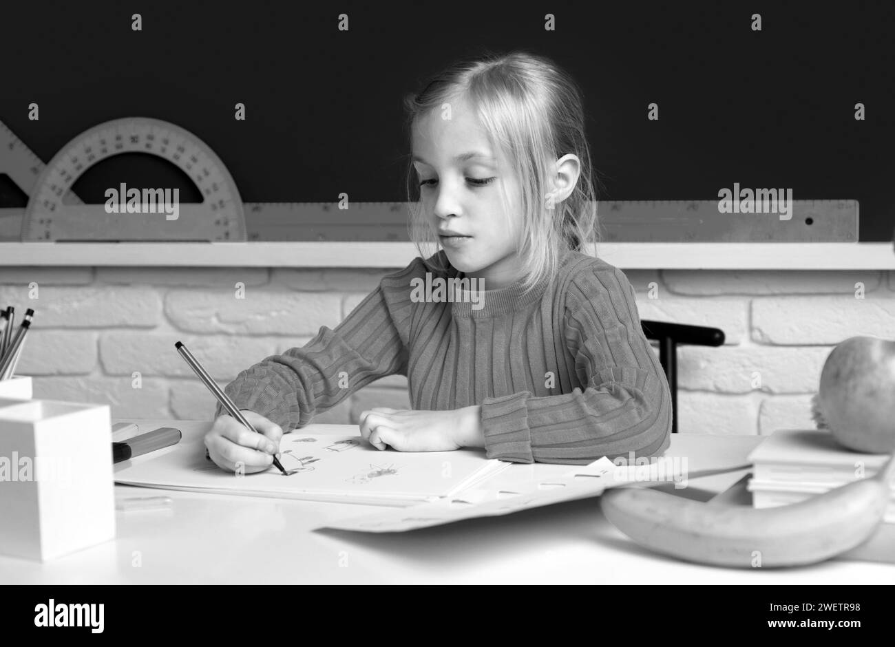 Portrait of cute little schoolgirl writing in book with classmates in ...