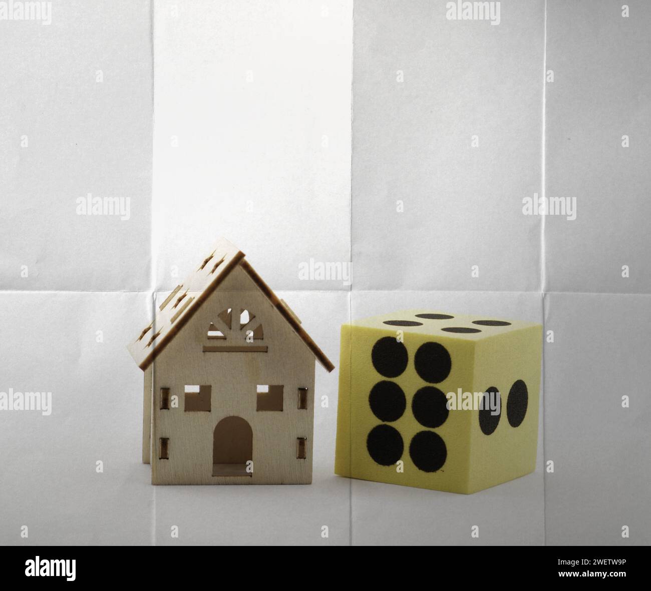 A macro photograph of a small toy house next to a yellow foam dice, set ...