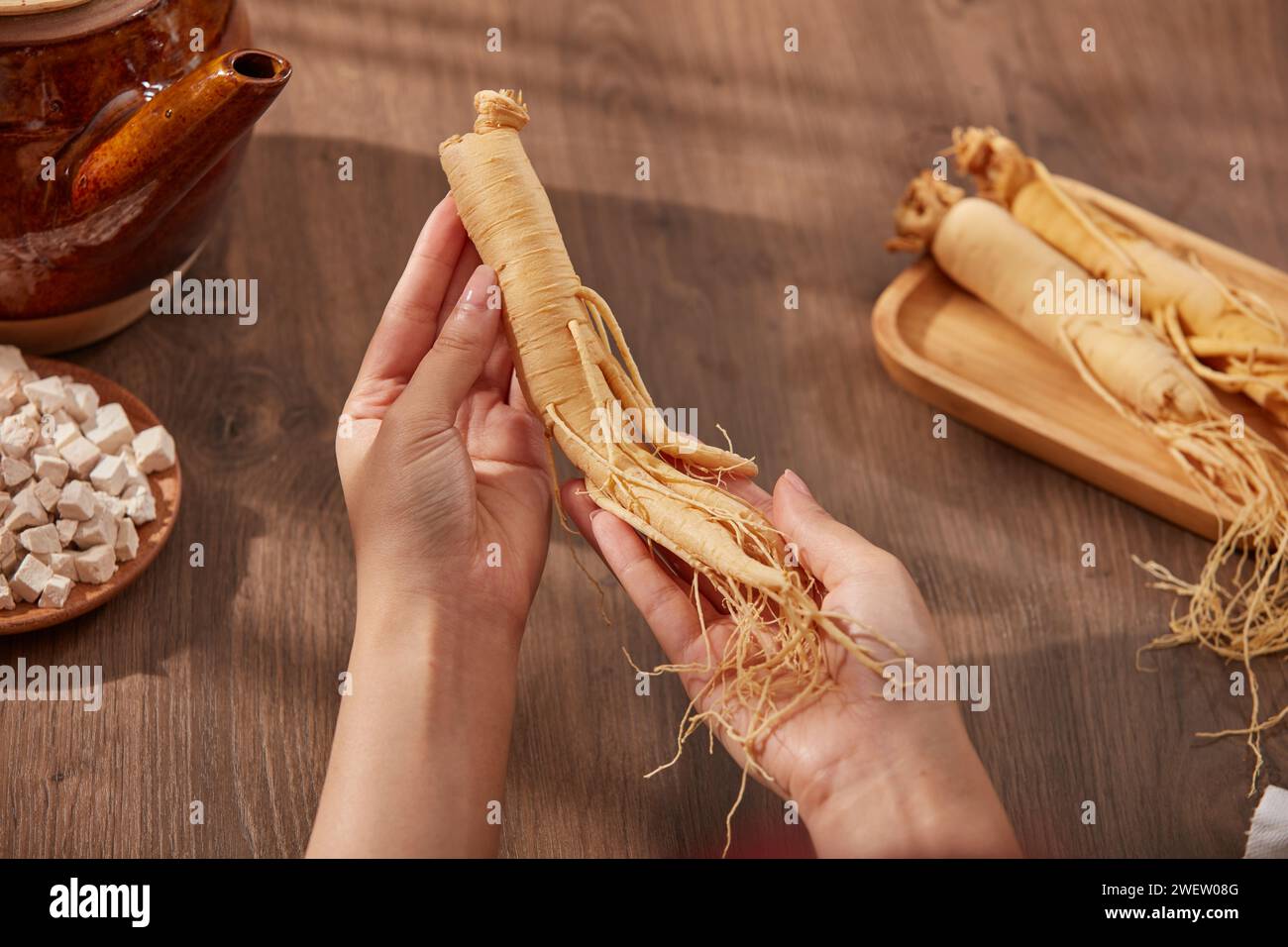 Ginseng tubers are lifted in woman's hand, herbs are placed on plate ...