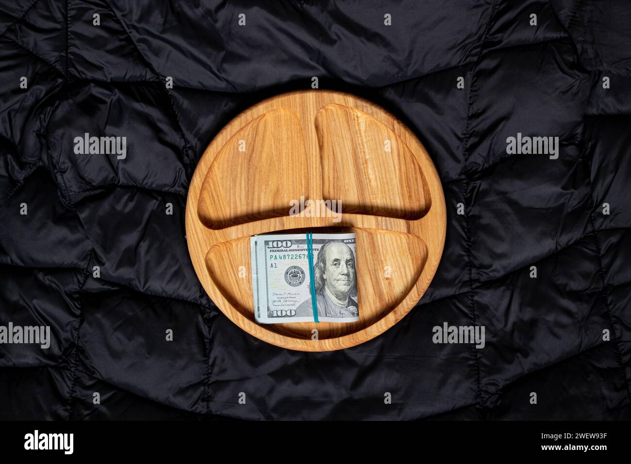 Wooden plate with one hundred dollar bills on a black background ...