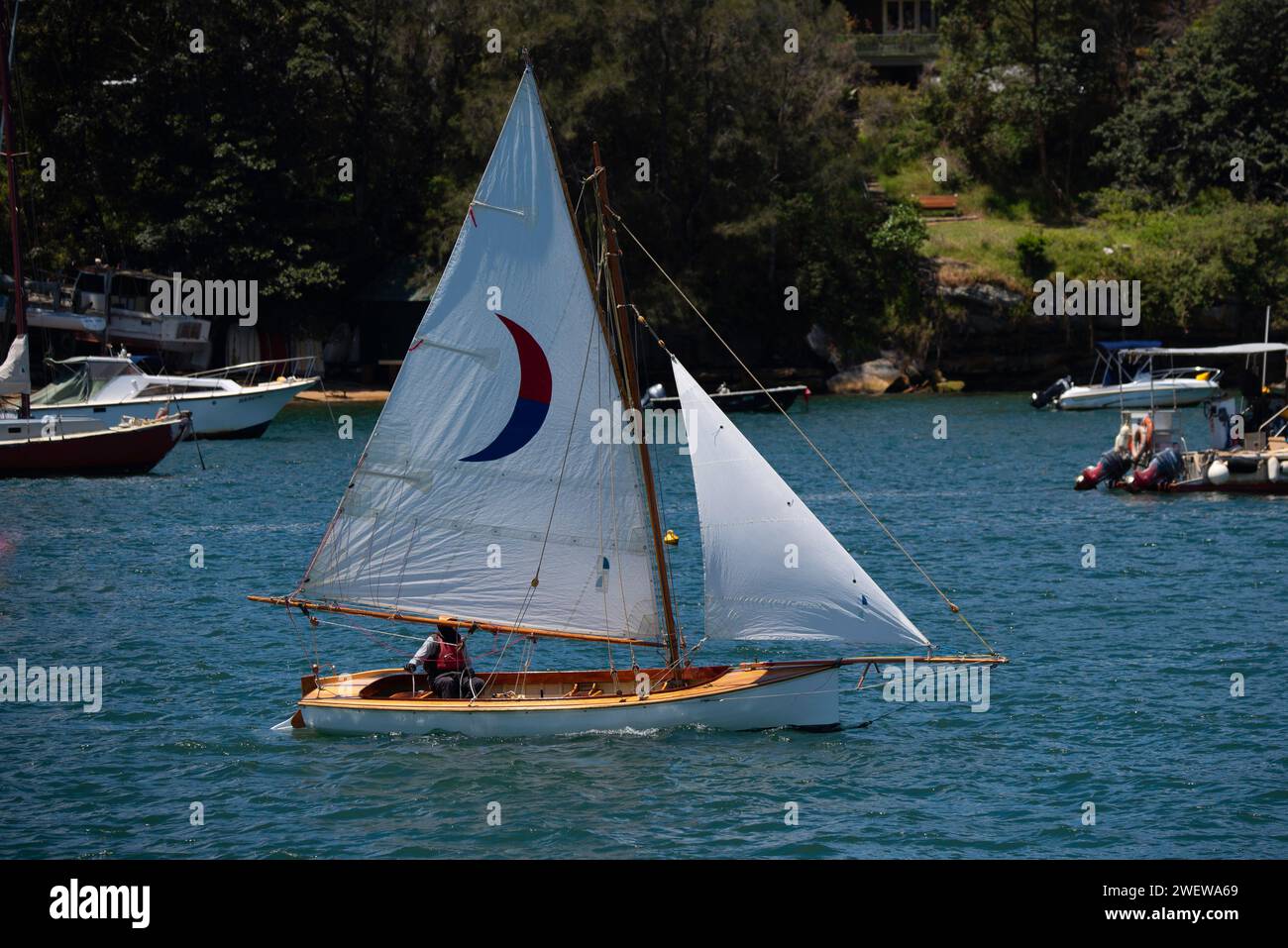 An open wooden sailing boat with a gaff rigged mainsail and jib sail ...