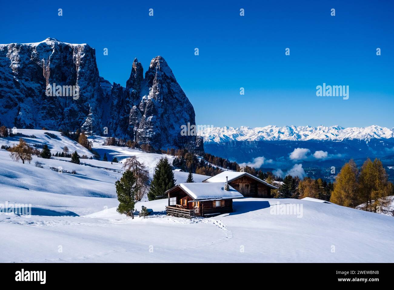 Hilly agricultural countryside with trees, wooden huts and snow-covered ...