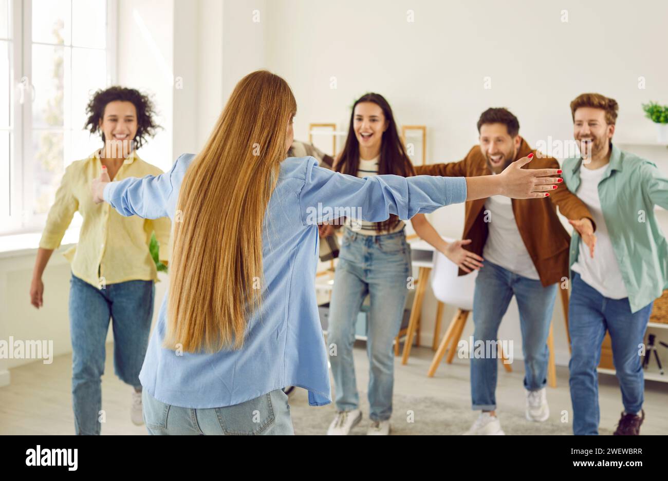 Girl standing back opened her arms greeting young happy friends at home ...