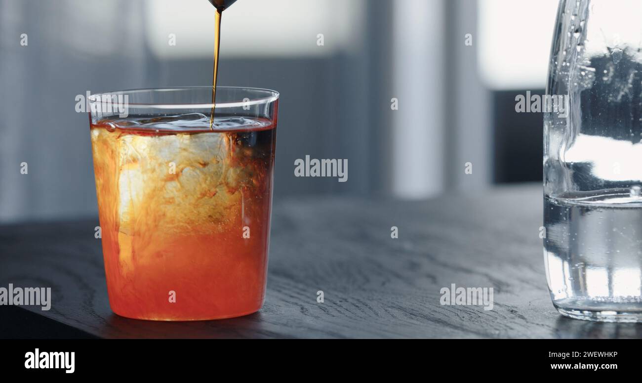 man pour syrup into tonic water with clear ice ball in tumbler glass on ...