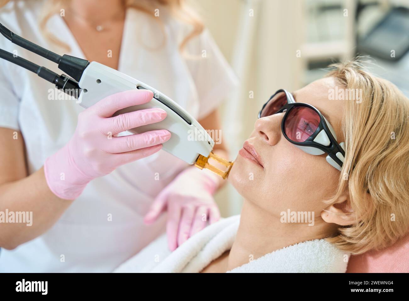 Partial female cosmetologist doing laser epilation of face of adult ...