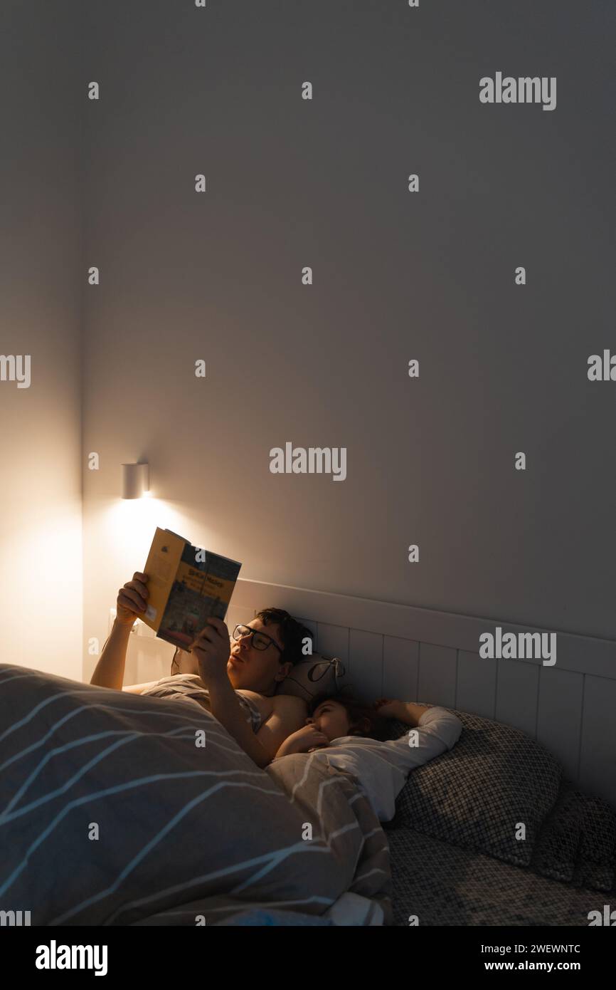 Adult reading a book in bed with child at night Stock Photo - Alamy