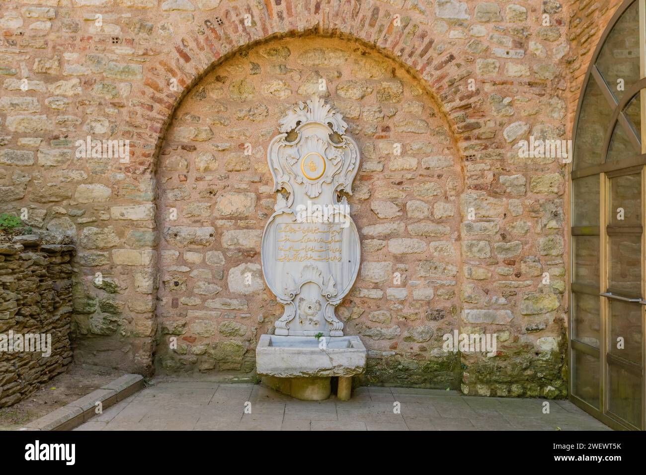 Water fountain with broken taps in shape of coat of arms against brick ...