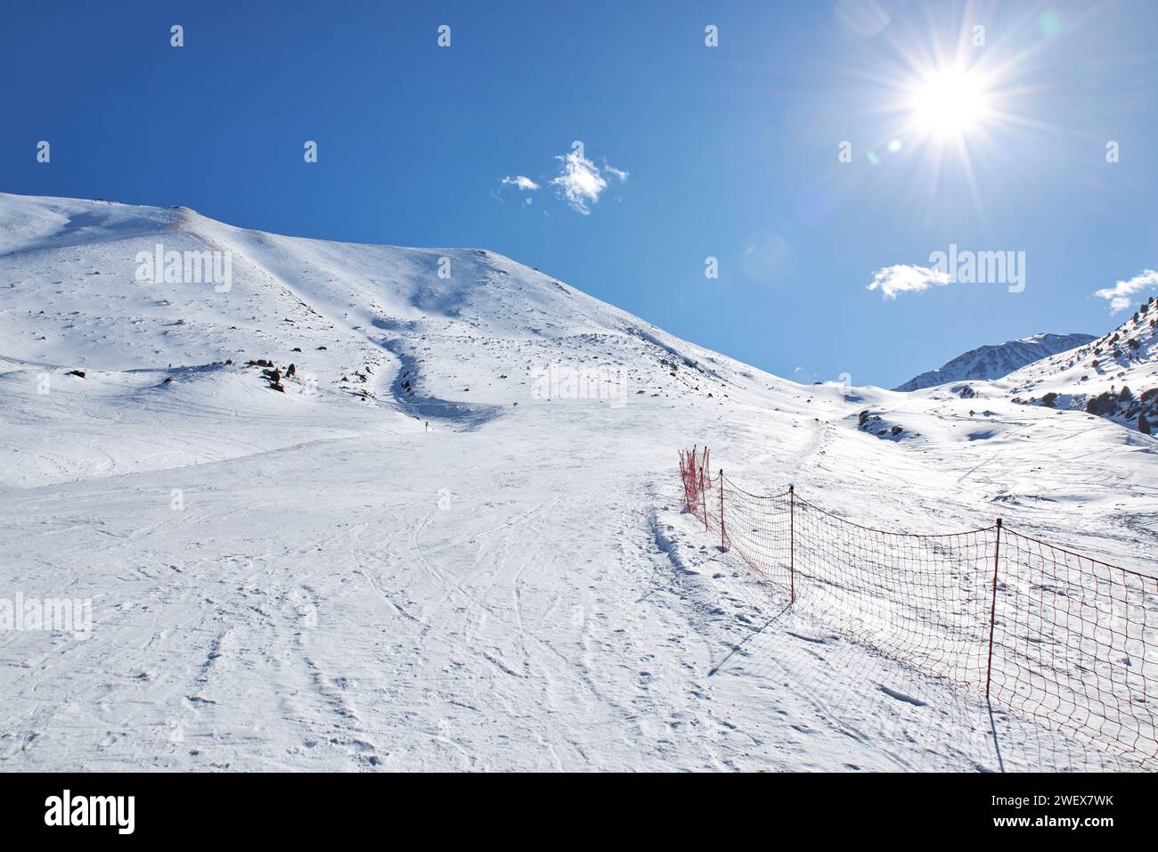Empty piste at ski resort, mountain slope. Red mesh fence marking the ...