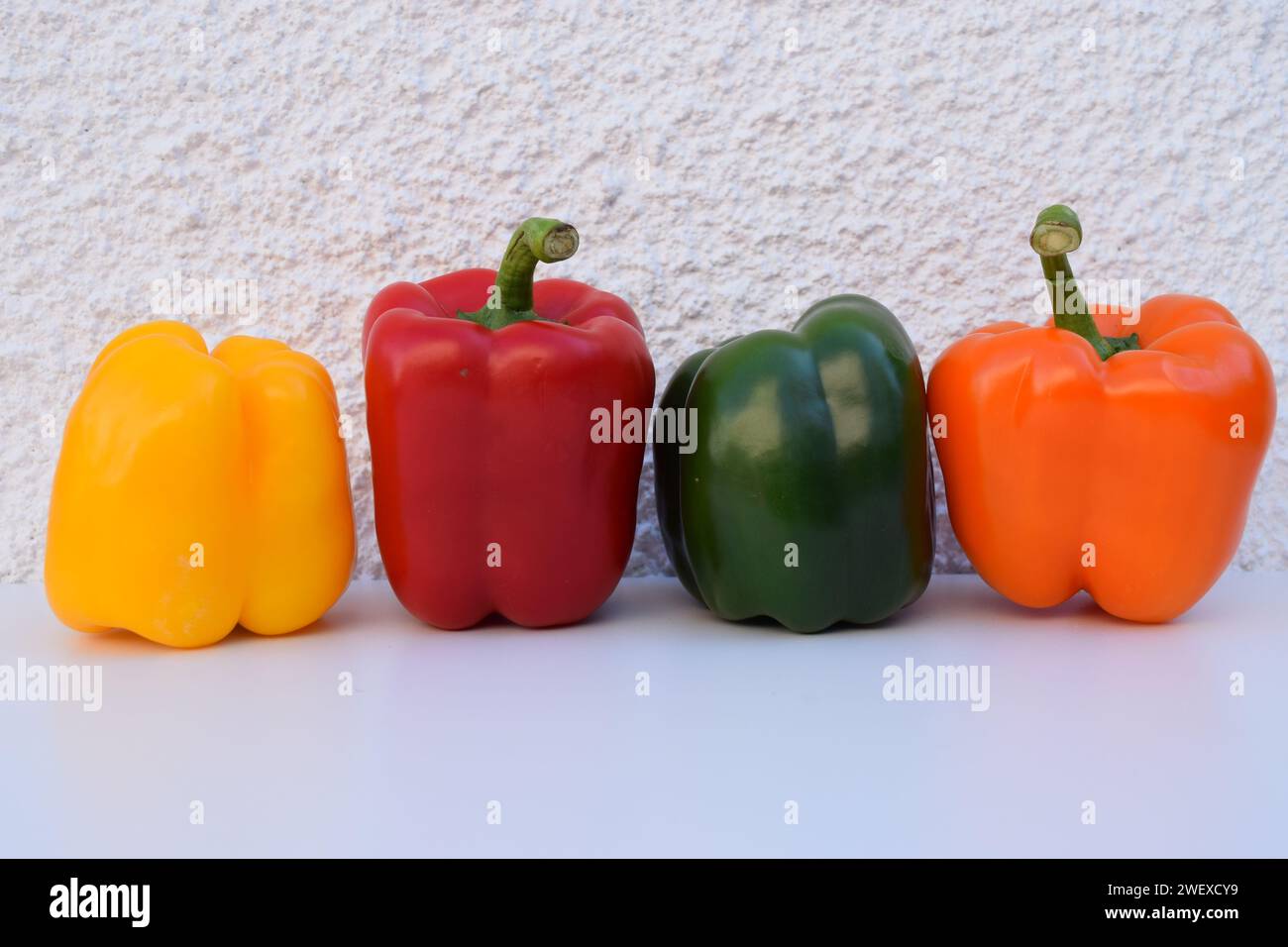 Four bell peppers in a row,sitting in front of a white wall background ...