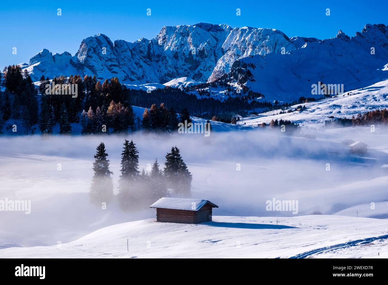Hilly agricultural countryside with fog, wooden huts and snow-covered ...
