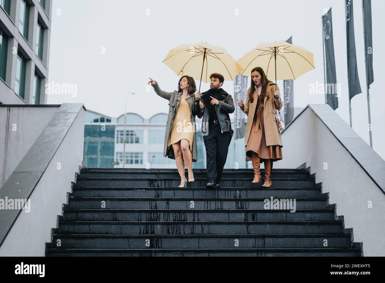 Three business partners with umbrellas descend city stairs on a rainy ...
