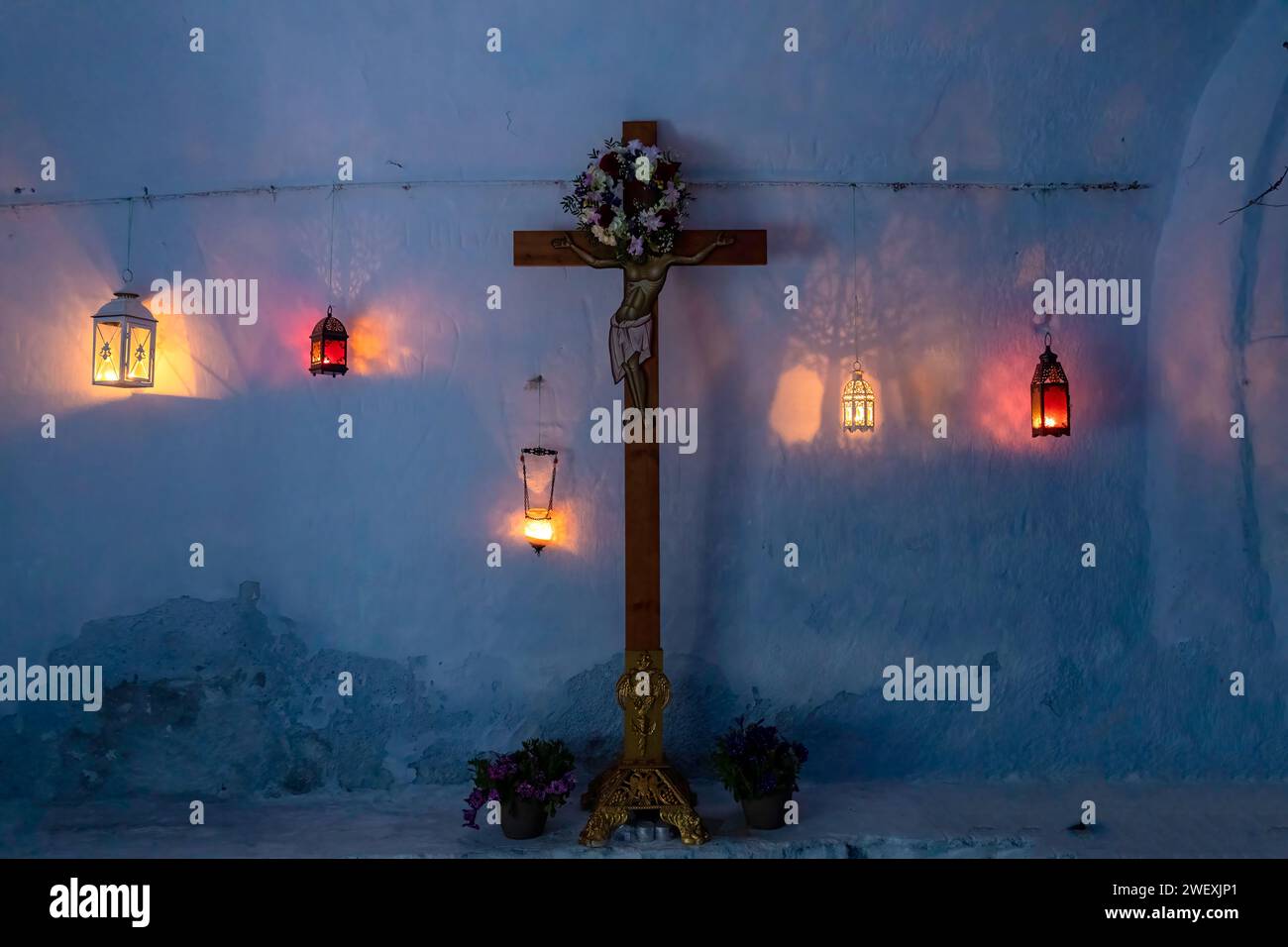 Christian cross with light lanterns hanging on a pale blue wall, during ...