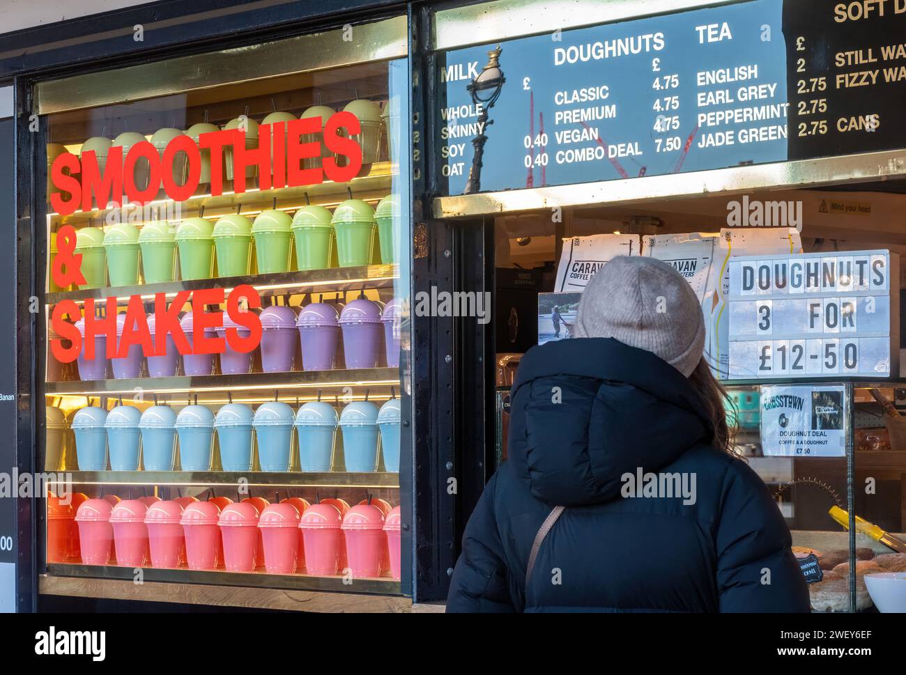 Customer at a refreshment kiosk with a display of colourful smoothies ...