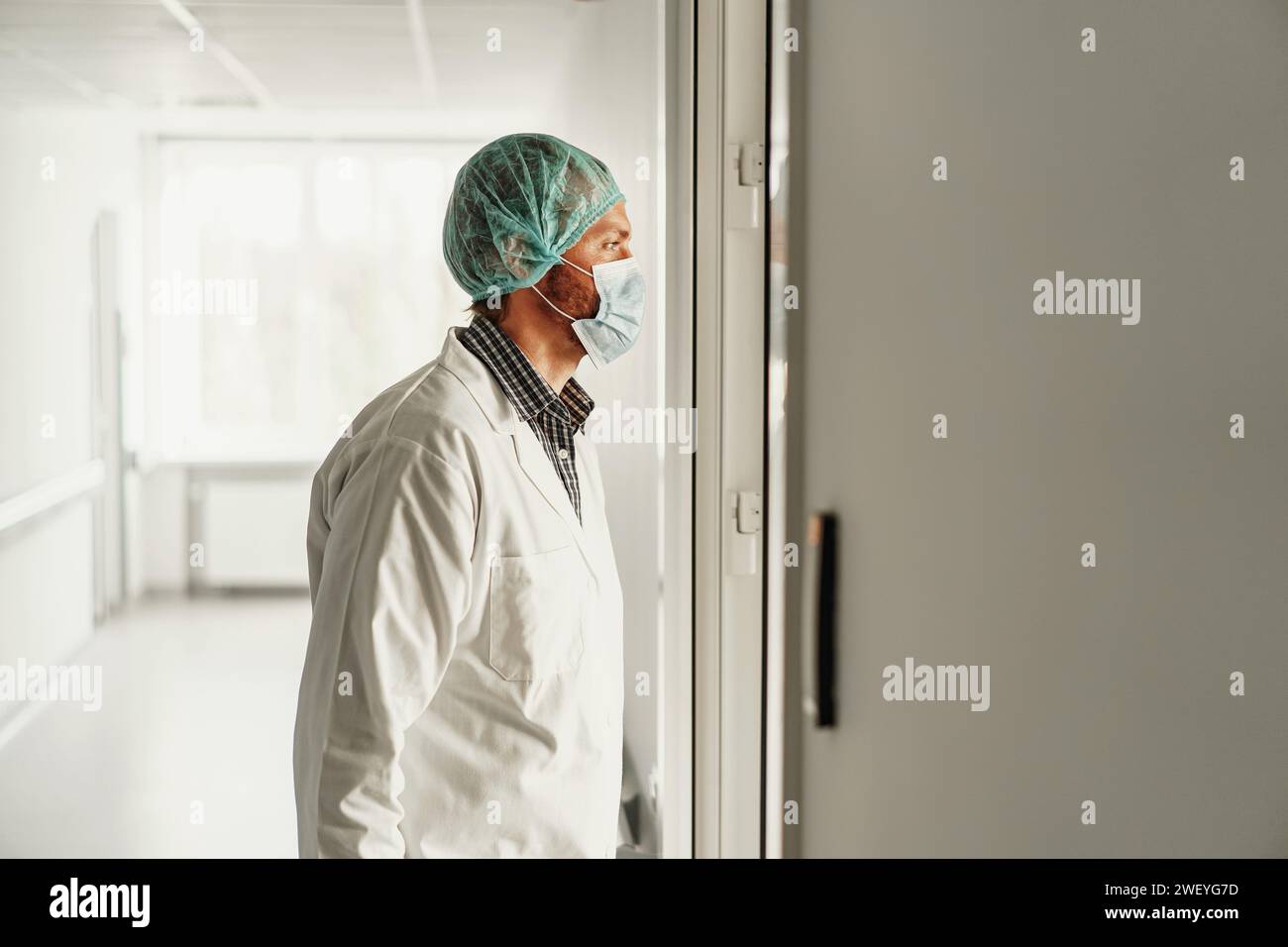 Male doctor in uniform and mask standing in hospital hall and looks at ...