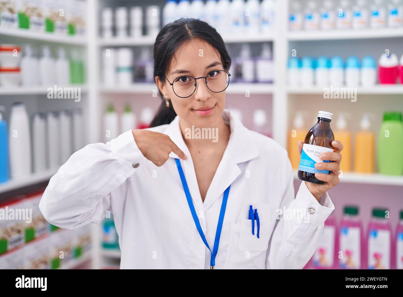 Young hispanic woman working at pharmacy drugstore holding syrup ...